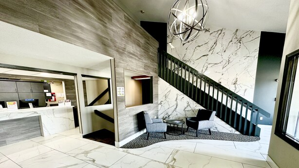 Um lobby moderno com balcão de recepção, piso de mármore, escada e área de estar.