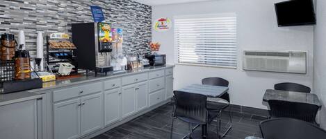 Cozinha moderna com armários cinzas, um espaço para café, um letreiro de café da manhã e uma TV montada na parede.