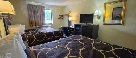 Quarto de hotel com duas camas, uma mesa de trabalho com televisão, uma luminária e uma janela com cortinas.