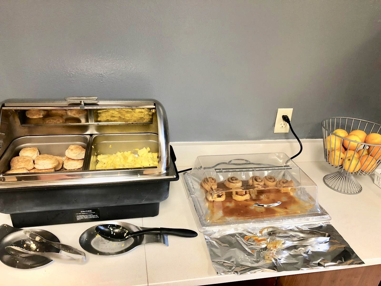 Uma mesa de buffet com diversos alimentos, incluindo biscoitos, purê de batatas e cinnamon rolls.