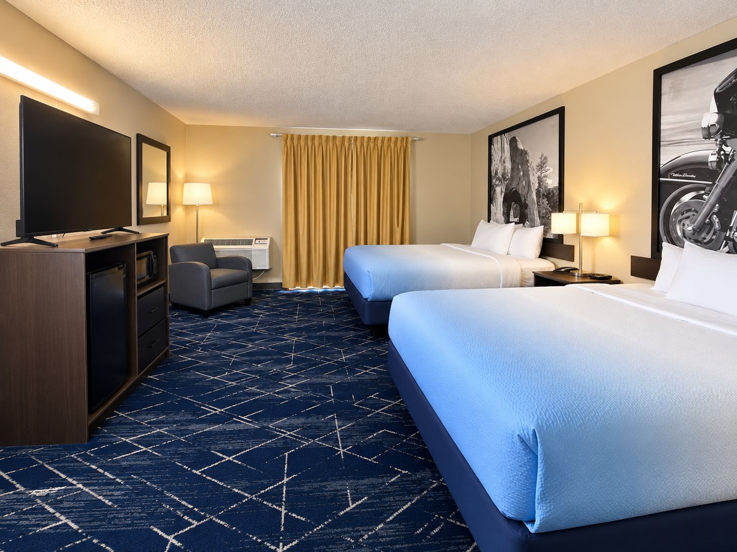 Quarto de hotel com duas camas, televisão, escrivaninha e uma cadeira.