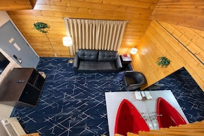 Um quarto com piso azul escuro estampado, sofá de couro preto, mesa pequena com abajur e banheira vermelha.