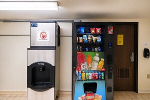 Máquina de vendas com diversas opções de lanches e bebidas, um botão para a geladeira e uma porta com placa indicando área de funcionários.