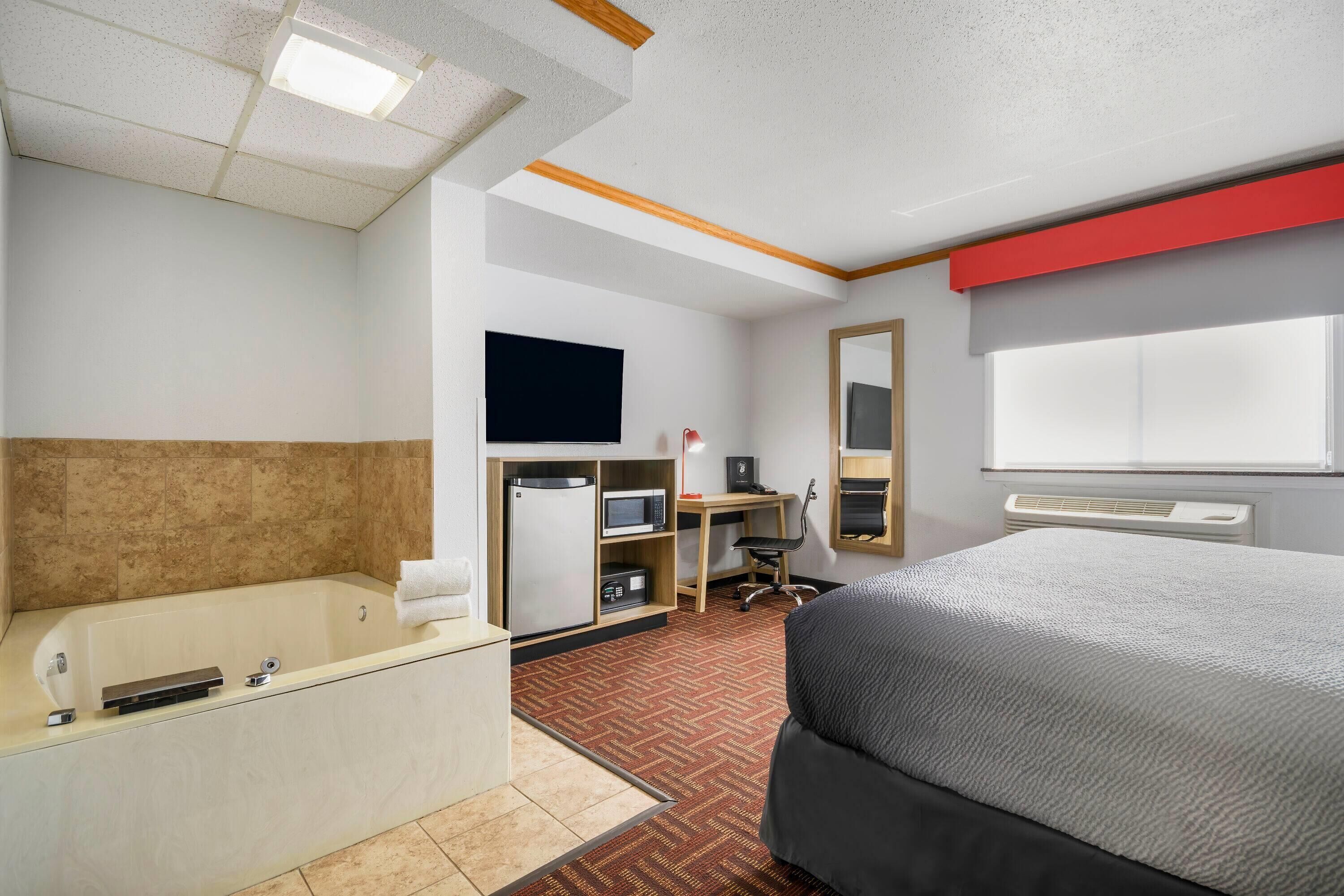 Quarto de hotel com uma cama grande, uma banheira, uma escrivaninha com computador, televisão e micro-ondas.