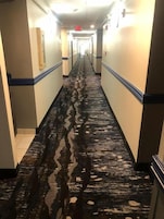 Corredor de hotel com chão molhado, paredes com detalhes em azul e portas em ambos os lados.