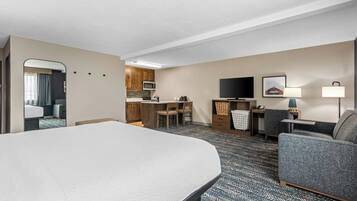 Quarto de hotel com cama grande, mesa de jantar, sofá, televisão, escrivaninha e cozinha compacta.