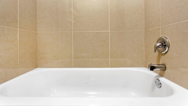 Um banheiro com banheira branca, paredes com azulejos bege e torneira cromada.