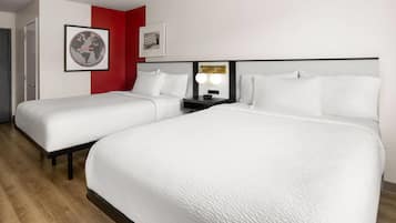 Quarto de hotel com duas camas, uma parede de destaque vermelha, um mapa-múndi emoldurado e uma mesa de cabeceira com abajur.
