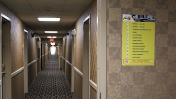 Um corredor de hotel com piso revestido de carpete, portas em ambos os lados e uma placa listando comodidades como quartos, sala de jogos e centro de negócios.