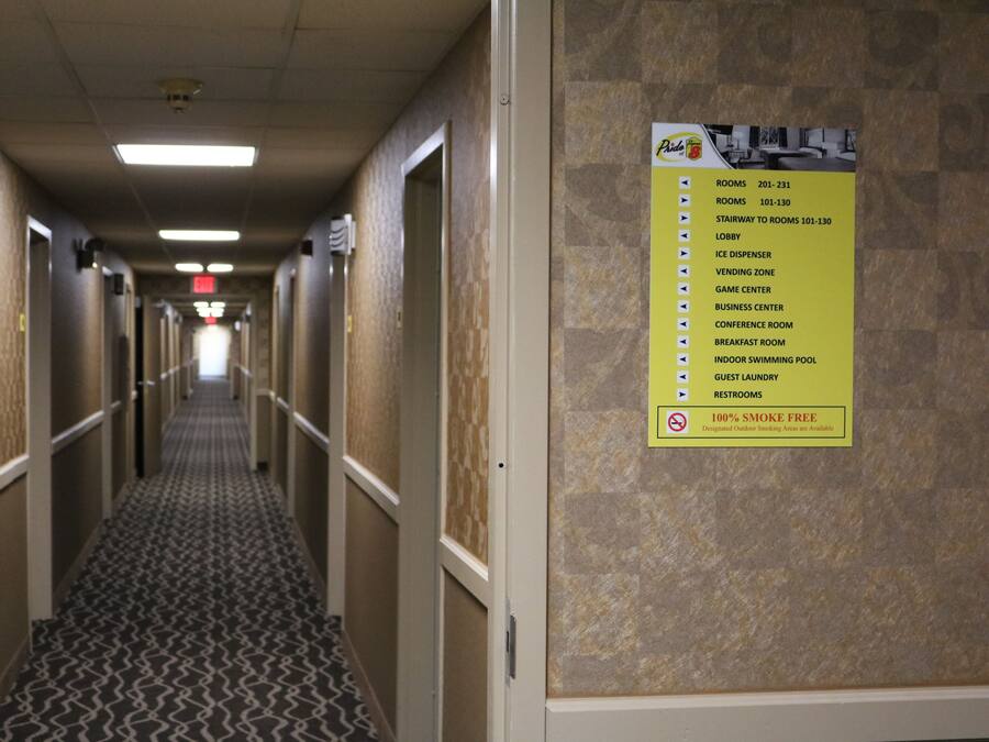 Um corredor de hotel com piso revestido de carpete, portas em ambos os lados e uma placa listando comodidades como quartos, sala de jogos e centro de negócios.