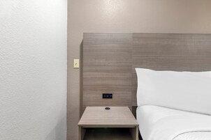 Quarto de hotel bem arrumado com uma cama, mesa de cabeceira e painel de controle fixado na parede.