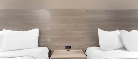 Quarto de hotel com duas camas, uma mesinha de cabeceira e painel de controle fixado na parede.