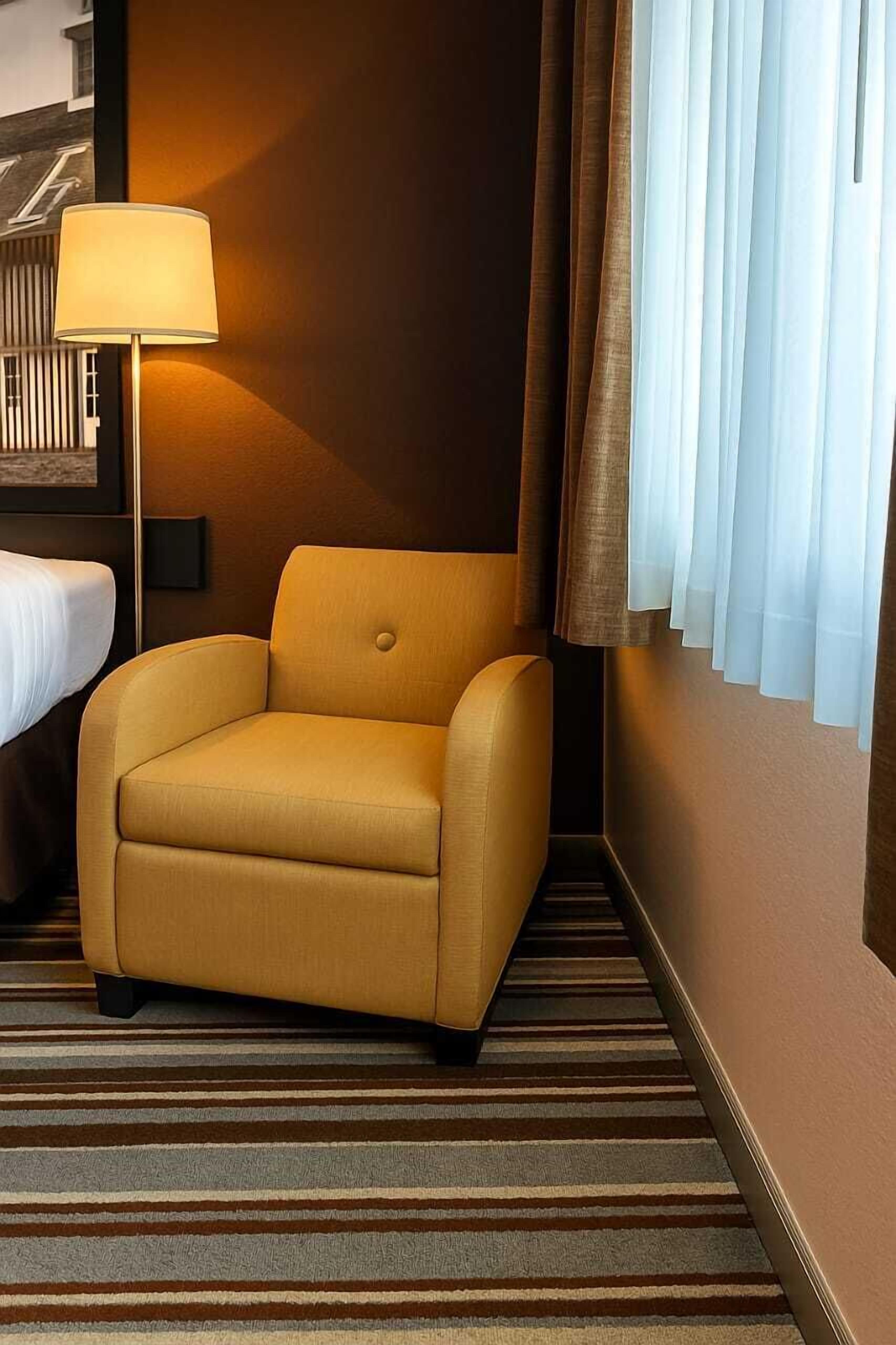 Quarto de hotel com carpete listrado, sofá, luminária e cama.