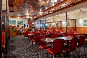 Um restaurante com assentos estofados em vermelho, mesas e vigas de madeira no teto, além de obras de arte nas paredes.