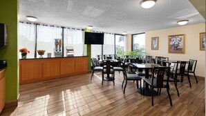 Restaurante com piso de madeira, balcão com televisão de tela plana e várias mesas e cadeiras.