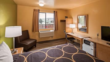 Quarto de hotel com cama, escrivaninha, cadeira, televisão, luminária, aquecedor e janela com cortinas.