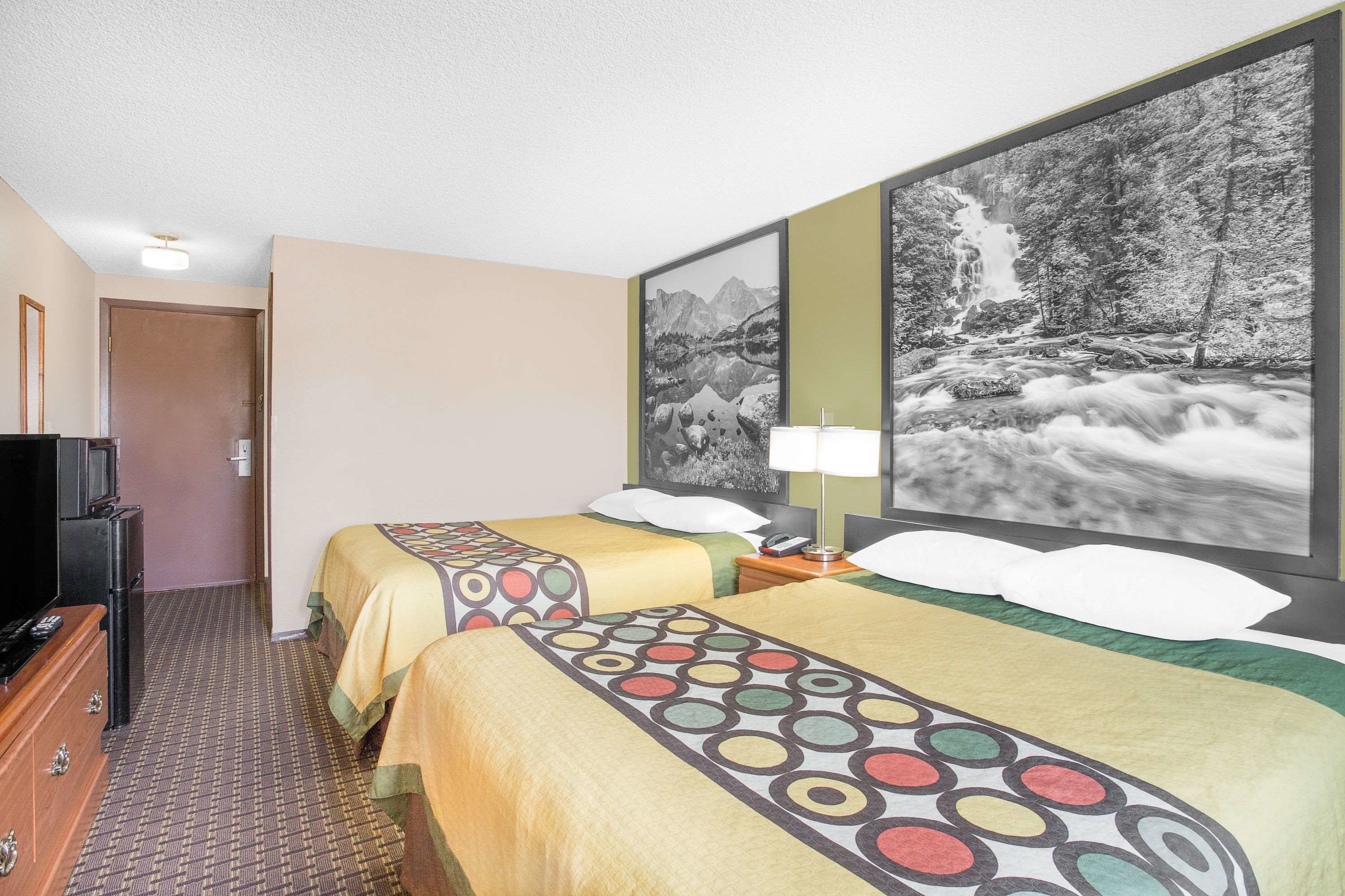 Quarto de hotel com duas camas, uma televisão e um quadro de uma paisagem de montanha.