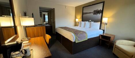 Quarto de hotel com cama, luminárias de cabeceira, escrivaninha com cafeteira, cadeira e um quadro na parede.