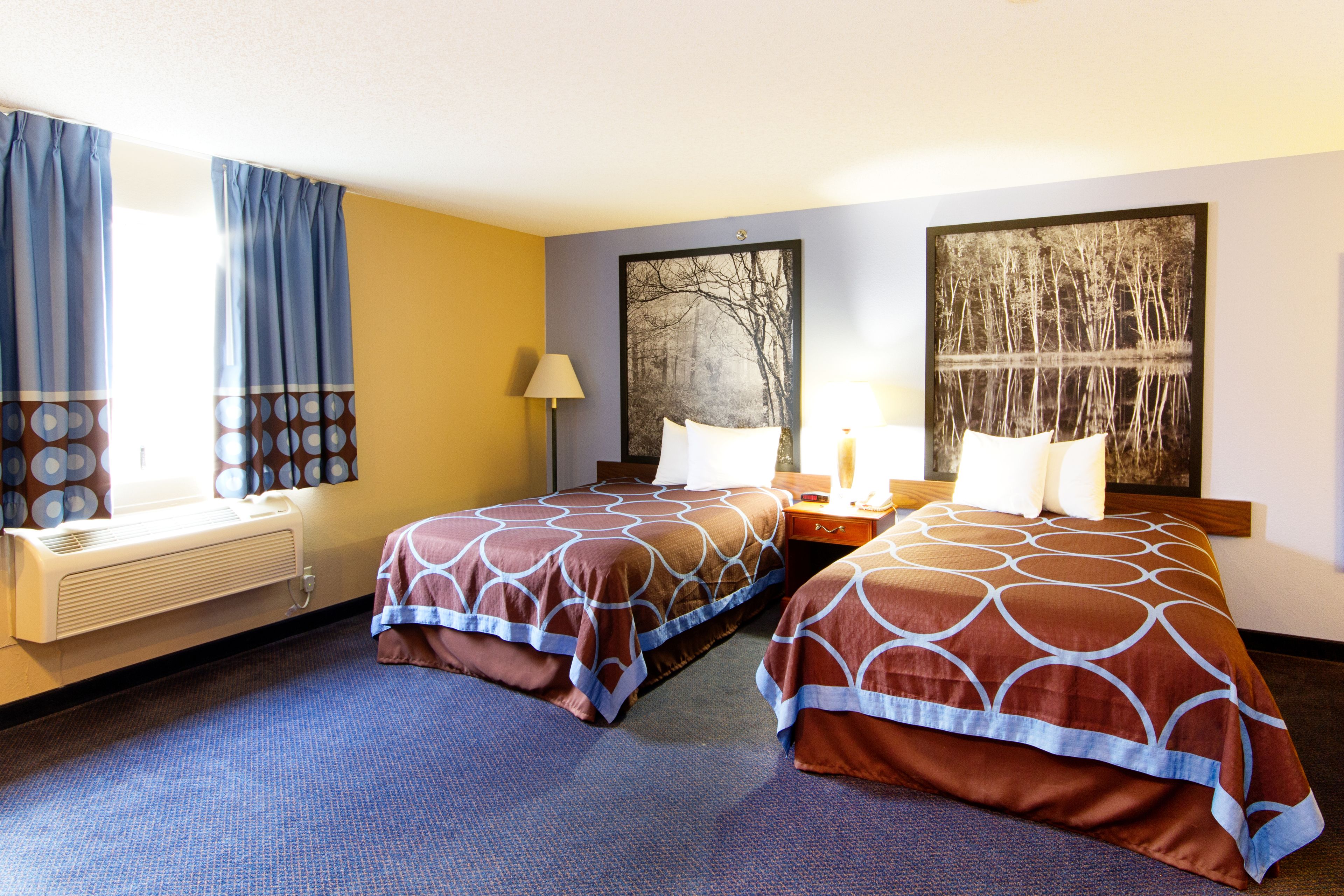Quarto de hotel com duas camas, uma janela com cortinas, um radiador e um quadro na parede.