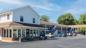Um motel com varanda frontal coberta, várias vagas de estacionamento e uma escadaria azul que dá acesso aos andares superiores.