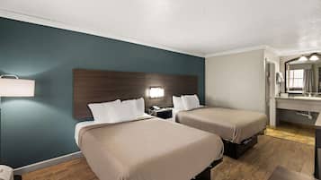 Quarto de hotel com duas camas, uma mesa de cabeceira, uma luminária, um espelho e um banheiro com pia e espelho.