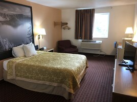 Quarto de hotel com uma cama grande, uma escrivaninha com um computador, ar condicionado e uma janela com cortinas.