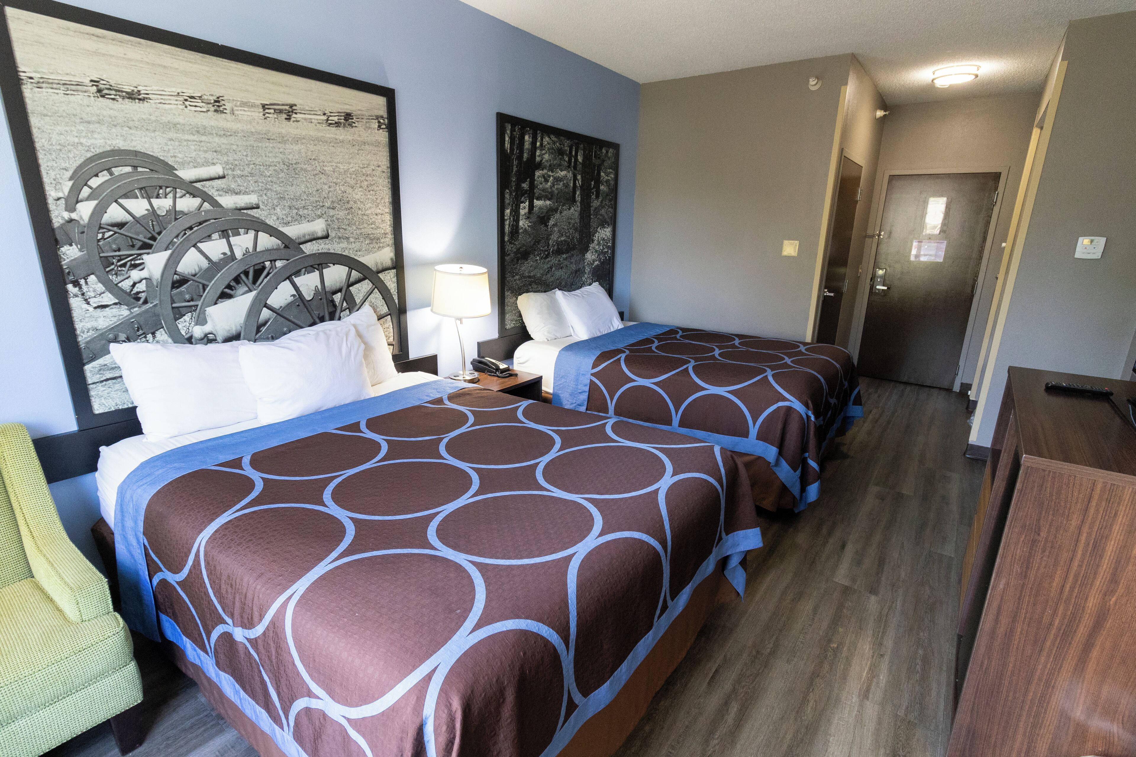 Quarto de hotel com duas camas, uma pintura grande de rodas, uma escrivaninha e um abajur.