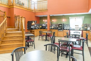 Restaurante com escadaria de madeira, várias mesas e cadeiras, área de cozinha e vista para o exterior.