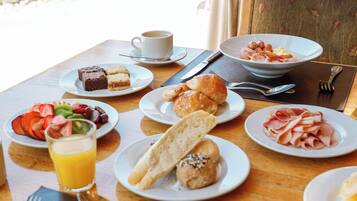 Mesa de café da manhã com diversos pratos, incluindo doces, frutas e uma xícara de café.