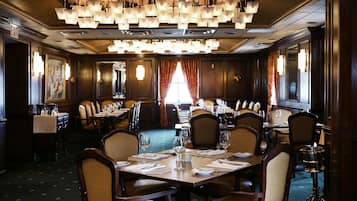 Uma sala de jantar formal com várias mesas, cadeiras e um candelabro.