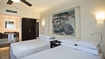 Quarto de hotel com duas camas, um quadro grande na parede, banheiro com espelho e ventilador de teto.