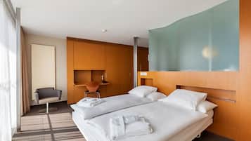 Quarto de hotel com uma cama grande, uma escrivaninha, uma cadeira e vista para o exterior.