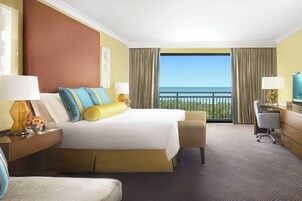 Quarto de hotel com cama, escrivaninha, cadeira, vista para o oceano e varanda.