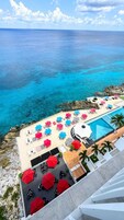 Uma área de piscina em resort com espreguiçadeiras e guarda-sóis, piscina e vista para o oceano.