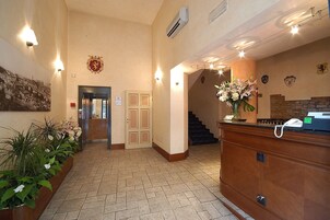 Um hall de hotel com uma recepção, uma escada e um brasão fixado na parede.