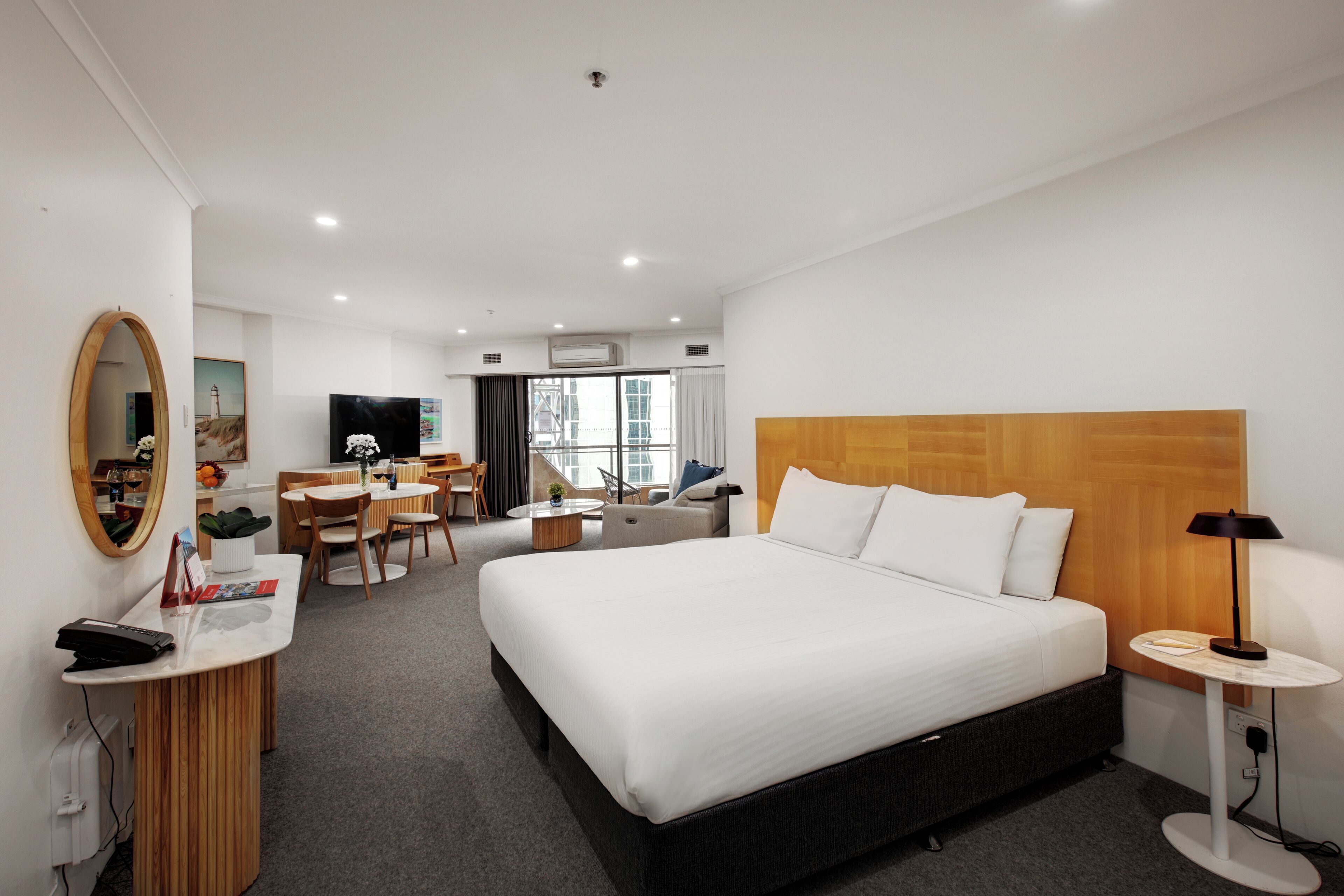 Quarto de hotel moderno com uma cama grande, uma escrivaninha, uma cadeira, uma mesa redonda e uma televisão.