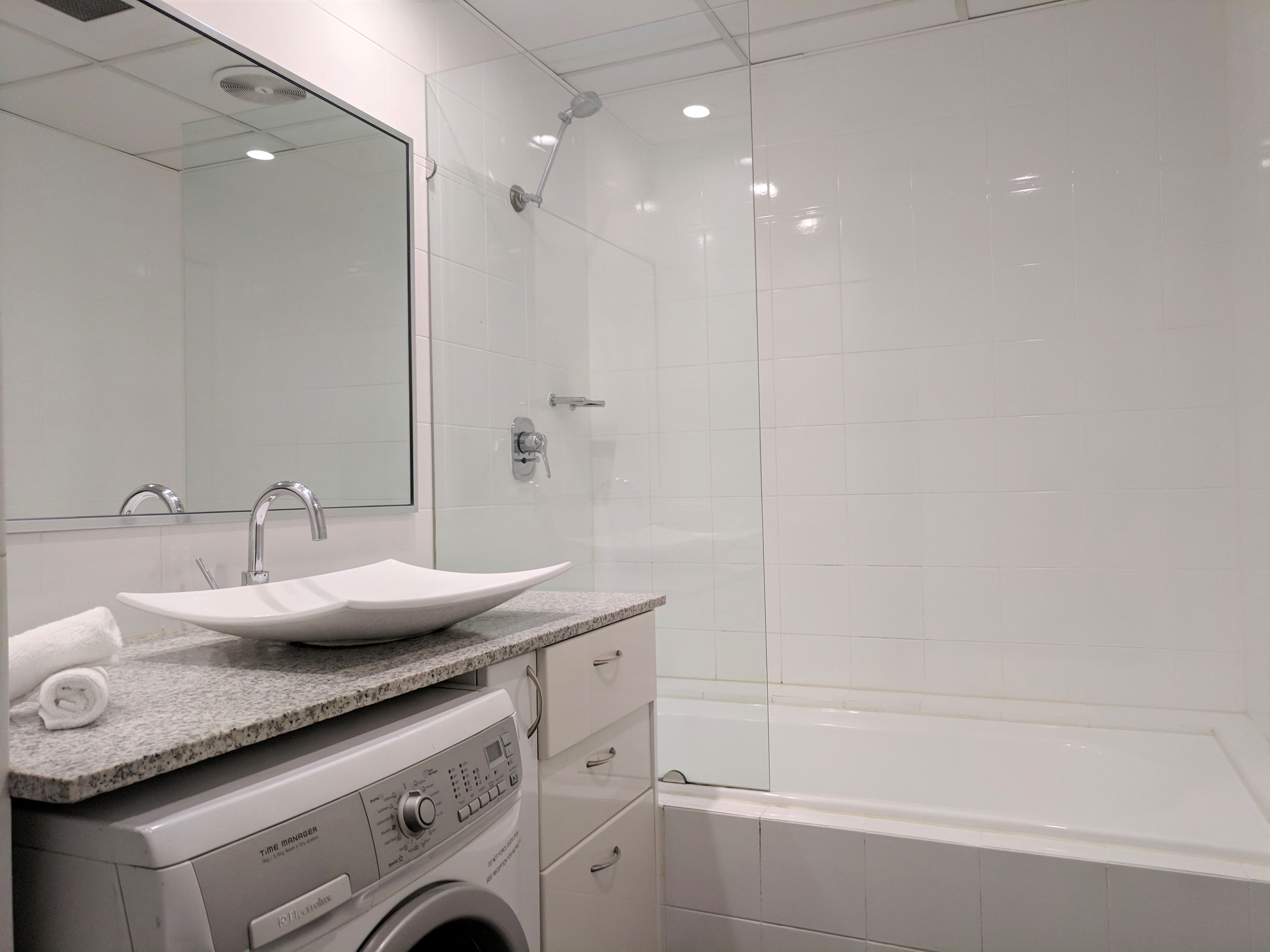 Uma casa de banho moderna com lavatório branco, máquina de lavar roupa embutida, chuveiro e banheira.