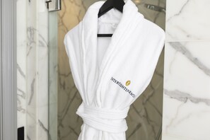 Robe branca com a inscrição "INTERCONTINENTAL" bordada, pendurada em um cabide preto em um banheiro com paredes de mármore.