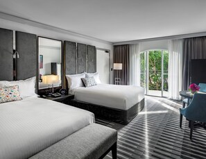 Quarto de hotel com duas camas, uma escrivaninha, uma cadeira e uma janela grande com vista para áreas verdes.