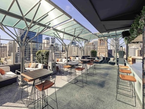 Um bar no terraço com mesas ao ar livre, vista para a cidade e design arquitetônico moderno.