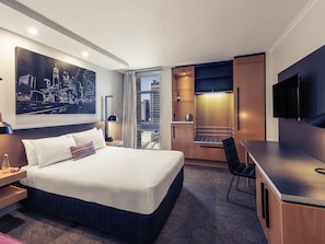 Quarto de hotel com cama, escrivaninha, televisão, quadro e vista para a cidade.