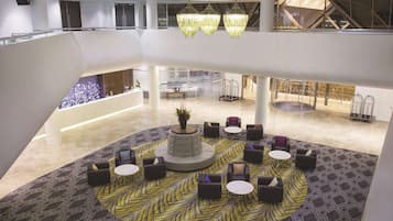Um hall amplo com área de estar central, balcão de recepção e escada para um andar superior.
