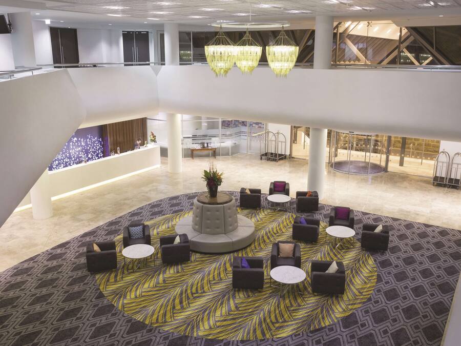 Um hall amplo com área de estar central, balcão de recepção e escada para um andar superior.