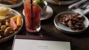 Uma mesa de pequeno-almoço com diversos pratos, uma bebida com rodela de limão e um menu intitulado "The Arms at The Lord Nelson Hotel Breakfast Menu Winter 2024".
