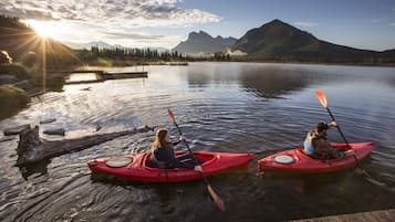 Dois caiaques num lago calmo com um cais de madeira e montanhas ao fundo.
