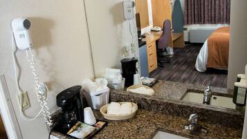 Quarto de hotel com bancada de granito, cafeteira, secador de cabelo e cama com cobertor marrom.