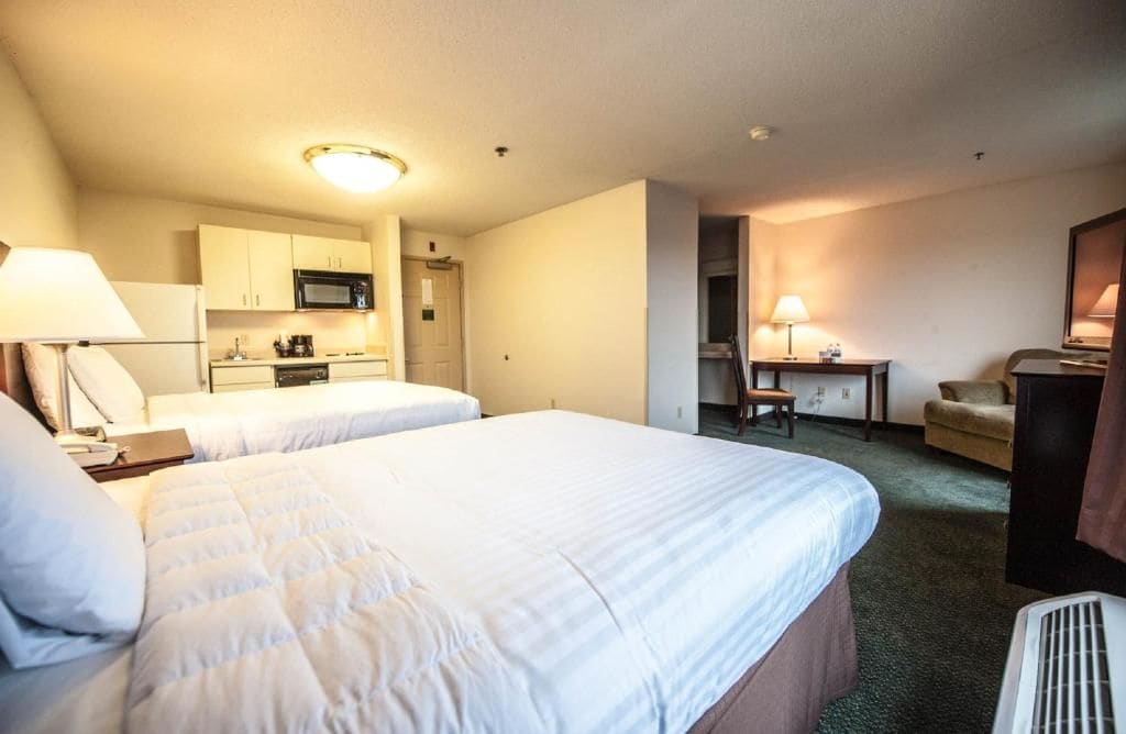 Quarto de hotel com duas camas, cozinha compacta, escrivaninha e uma cadeira.