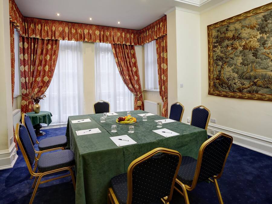 Uma sala de conferências com uma mesa verde, cadeiras azuis e um quadro na parede.