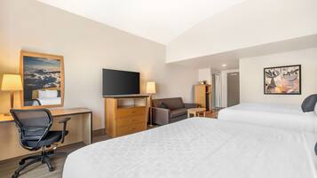Quarto de hotel com cama, escrivaninha, cadeira, televisão e obras de arte.
