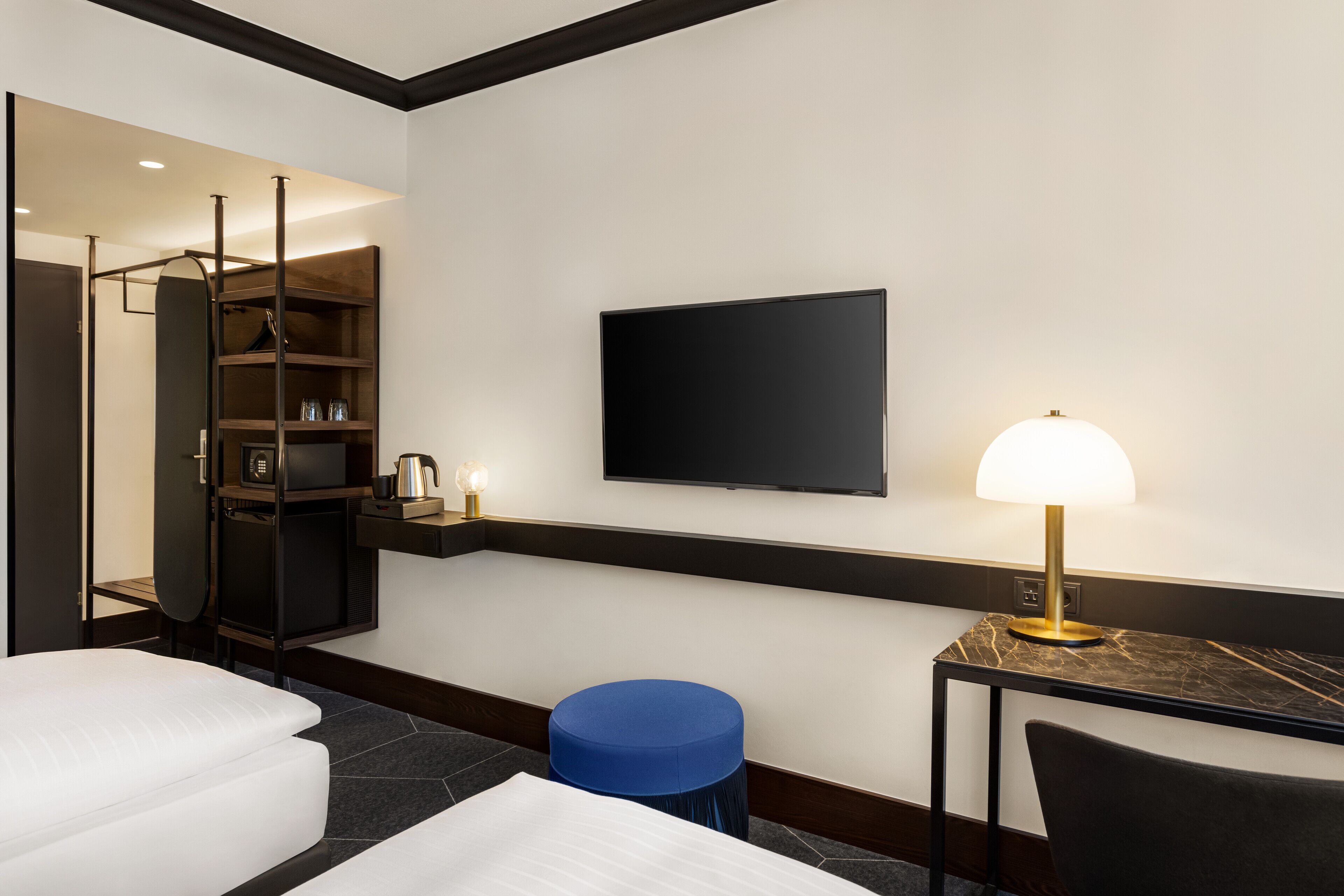 Quarto de hotel com cama, escrivaninha com luminária, televisão na parede e armário.